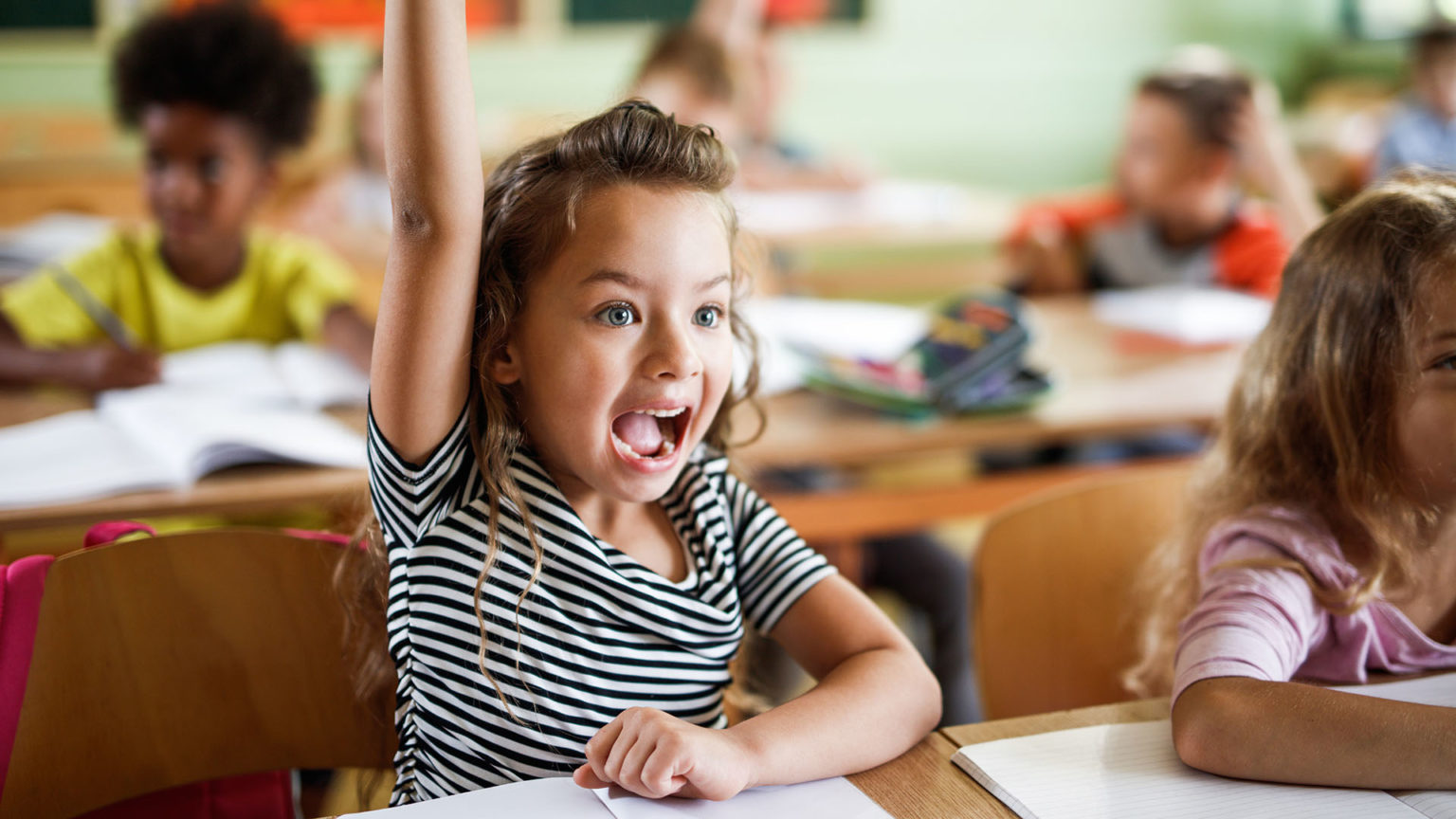 Happy schoolgirl raising her hand to answer the question on a class ...